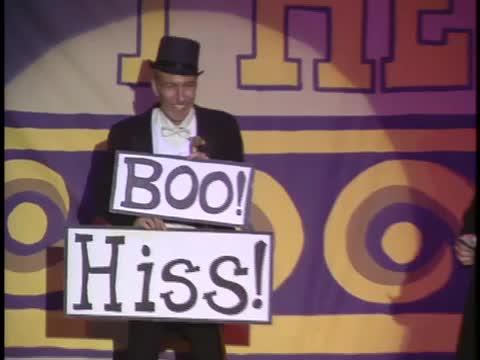 The villain in a melodrama holds up "boo" and "hiss" signs. - Wazee Digital